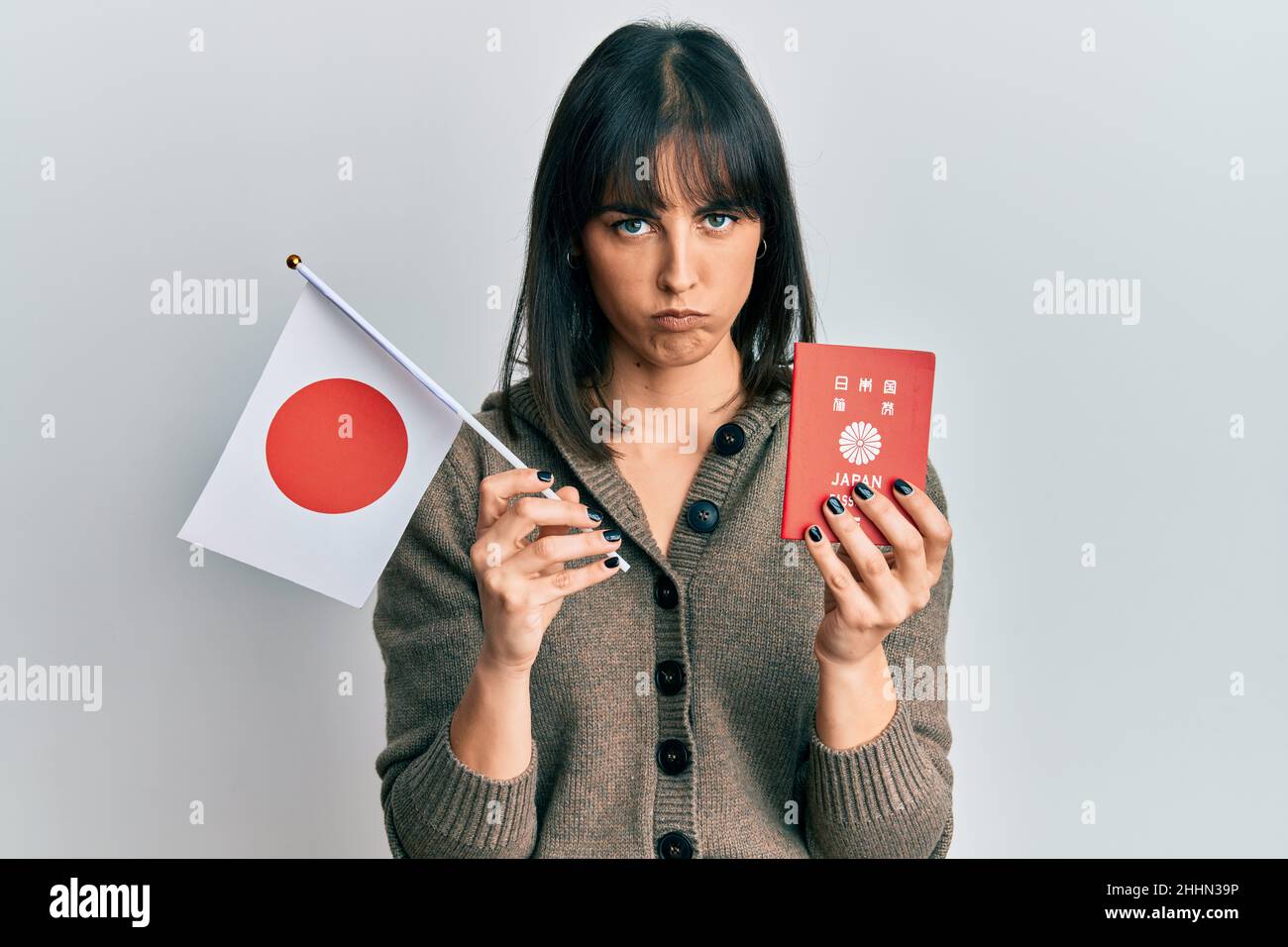 Young hispanic woman holding japan flag and passport depressed and ...