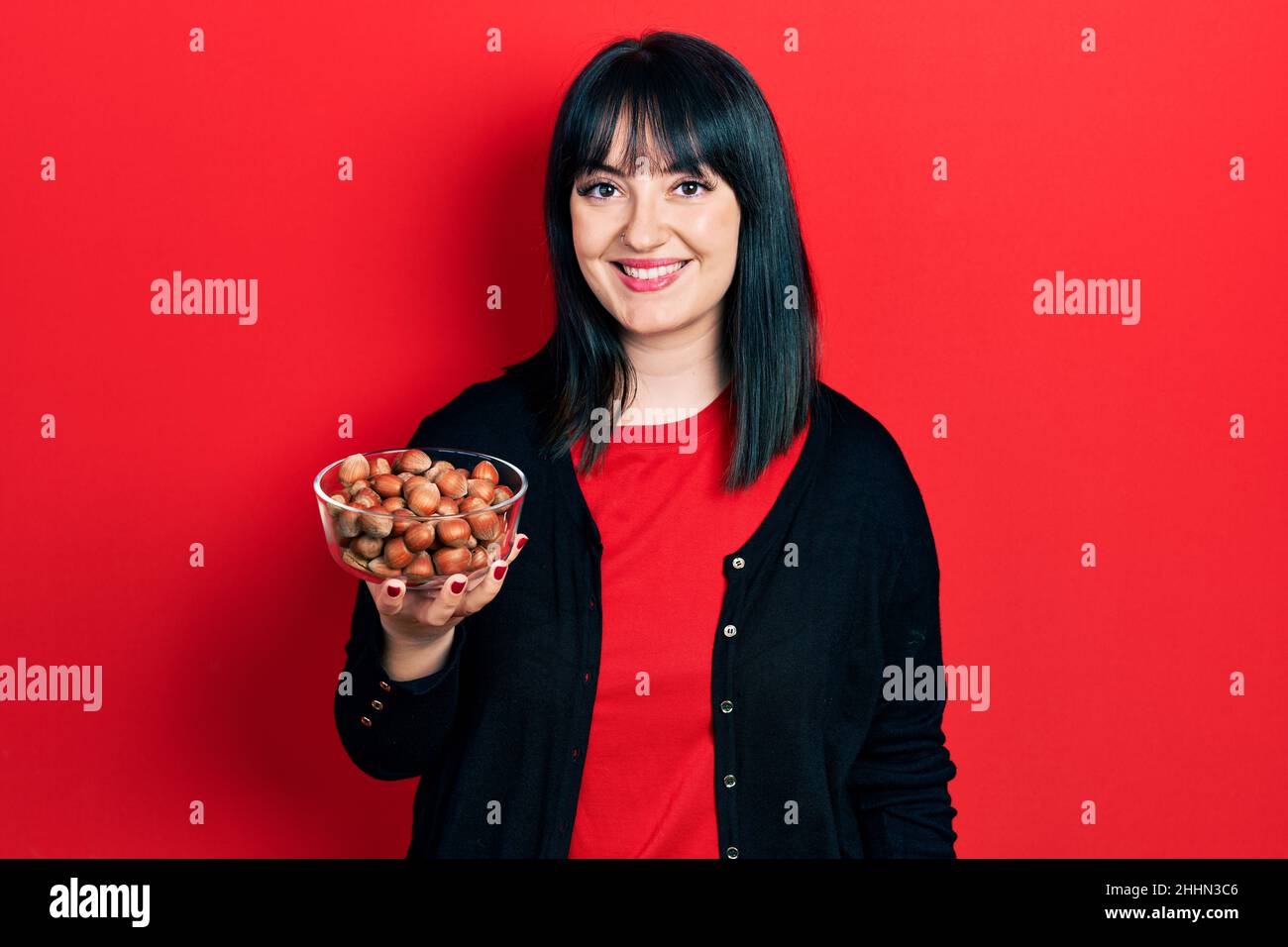 Young hispanic woman holding bowl of chestnuts looking positive and ...