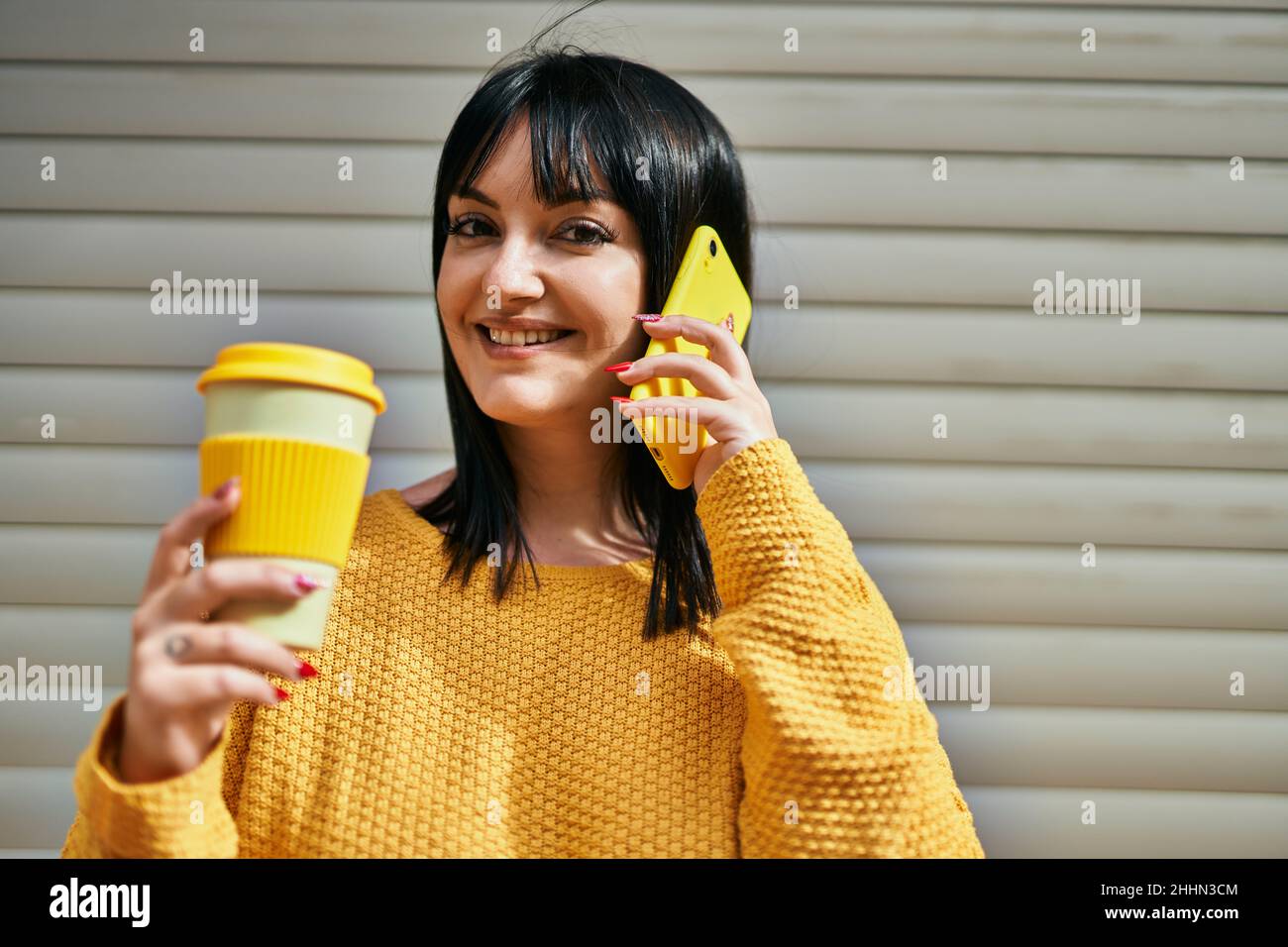Young brunette woman speaking on the phone and drinking a cup of coffee ...