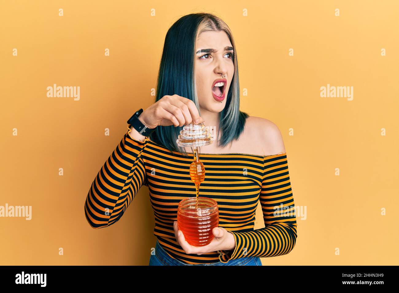 Young modern girl holding honey angry and mad screaming frustrated and ...