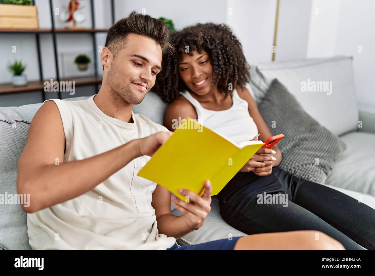 Man and woman couple using smartphone reading book at home Stock Photo ...