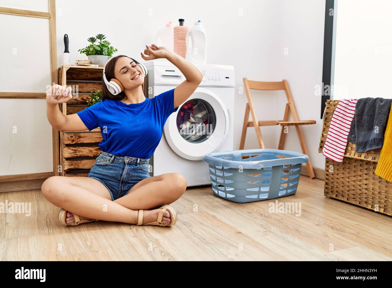 Young caucasian woman listening to music waiting for washing machine at ...