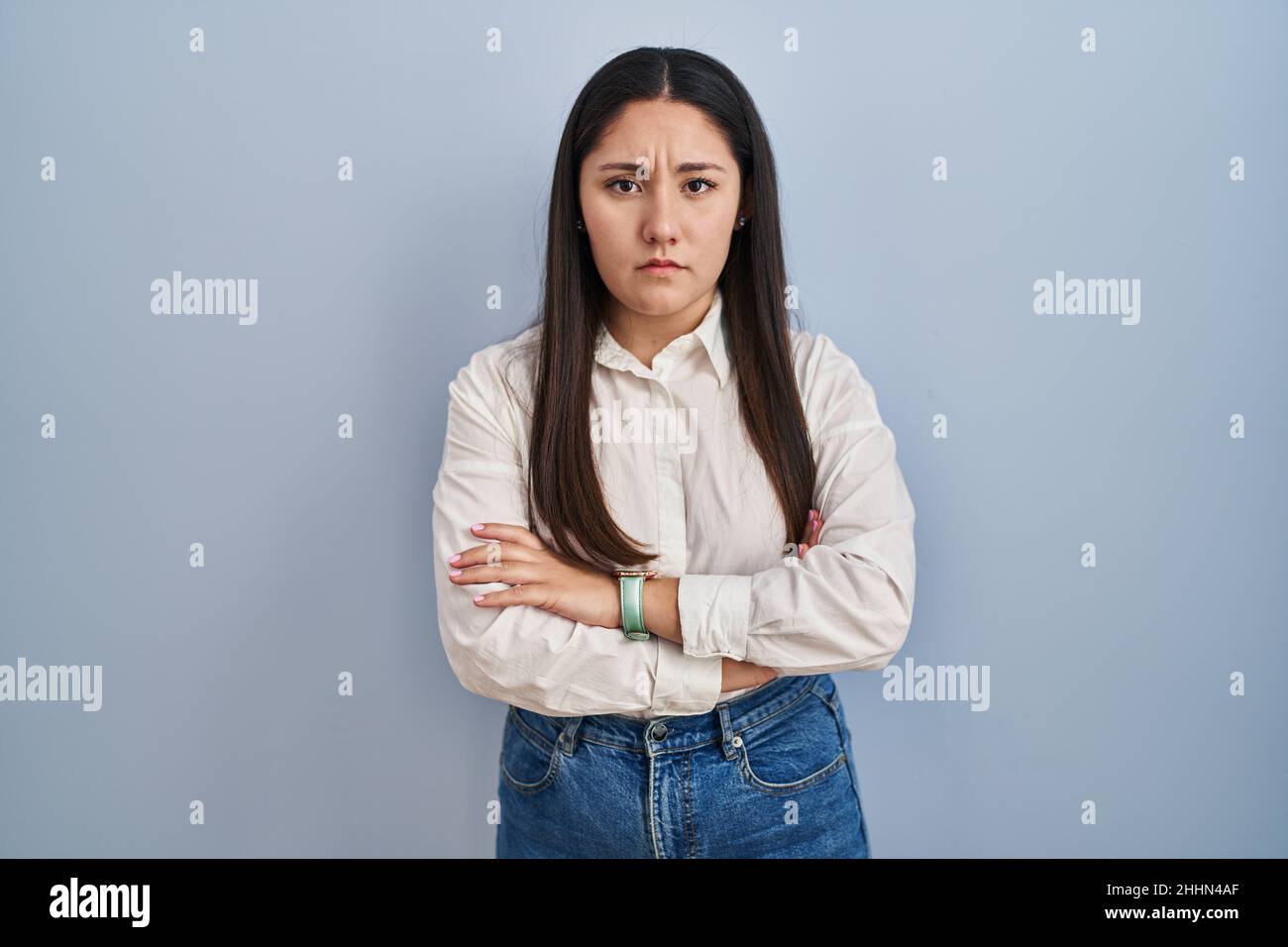 Young latin woman standing over blue background skeptic and nervous ...