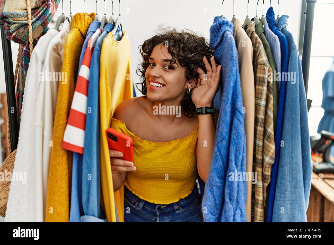 Young hispanic woman searching clothes on clothing rack using ...