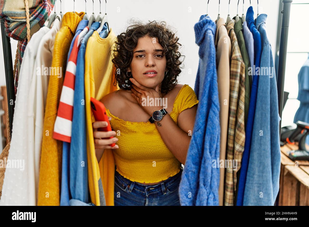 Young hispanic woman searching clothes on clothing rack using ...