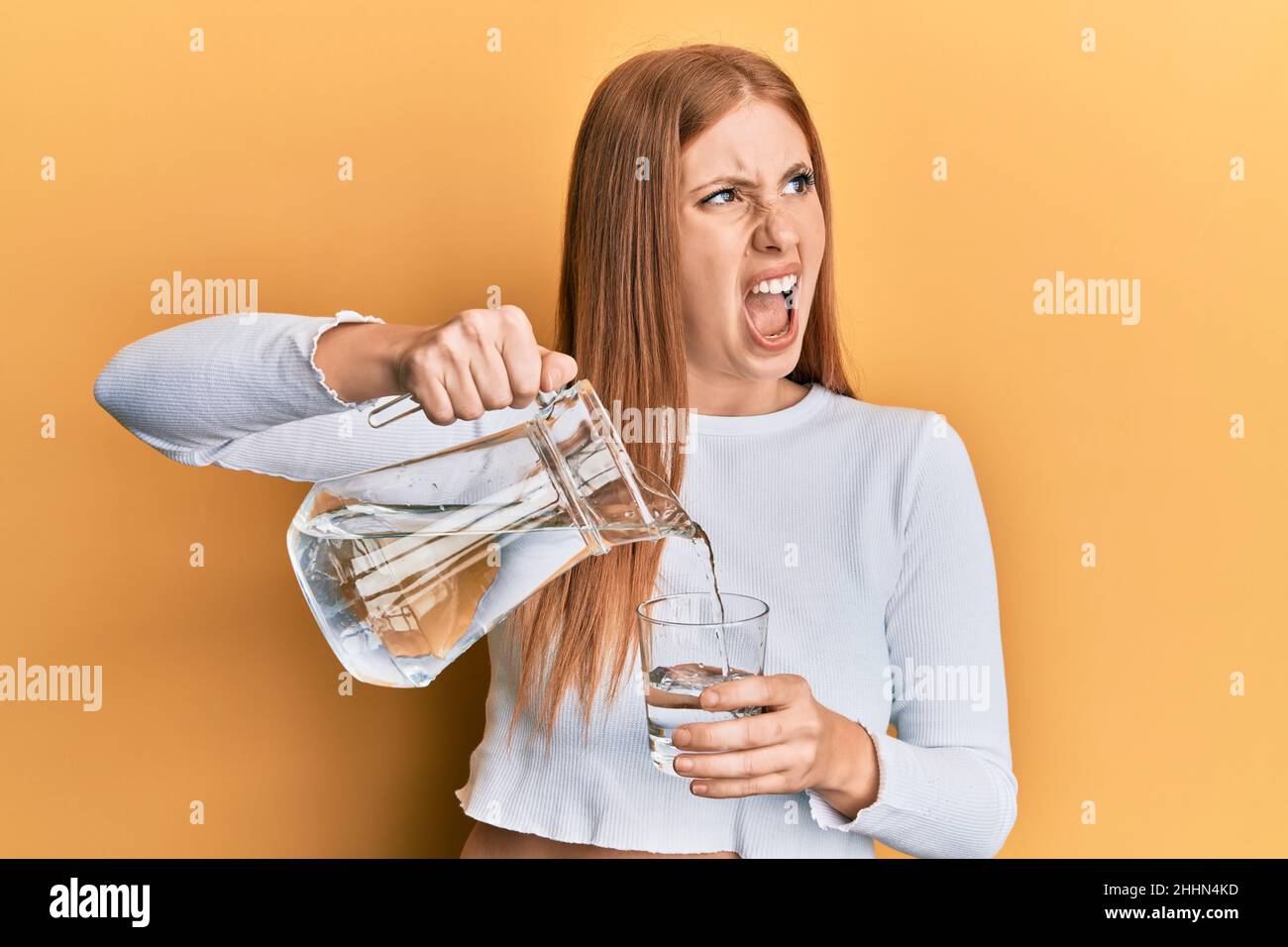 Young irish woman pouring water angry and mad screaming frustrated and ...