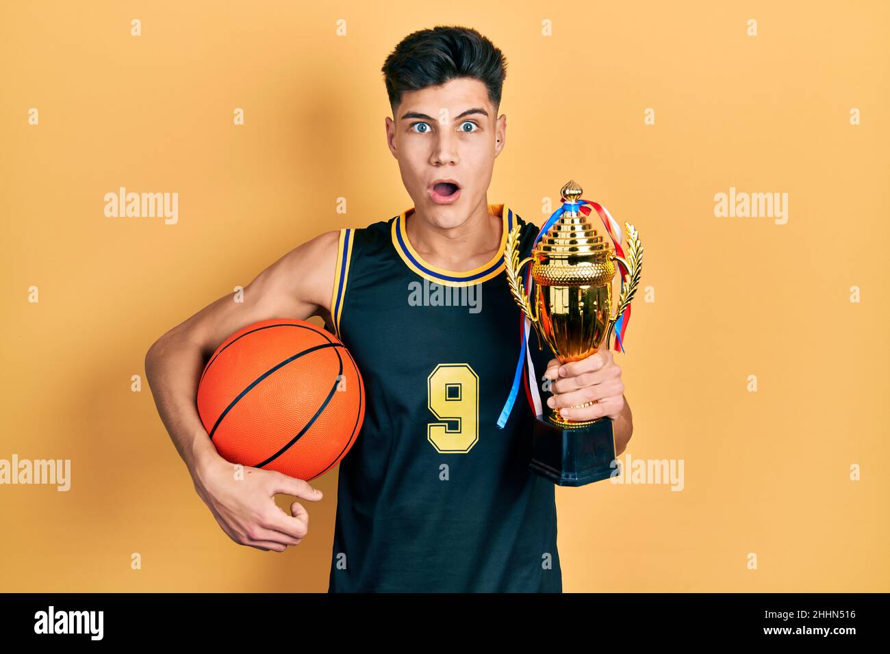 Young hispanic man wearing basketball uniform holding ball and prize ...