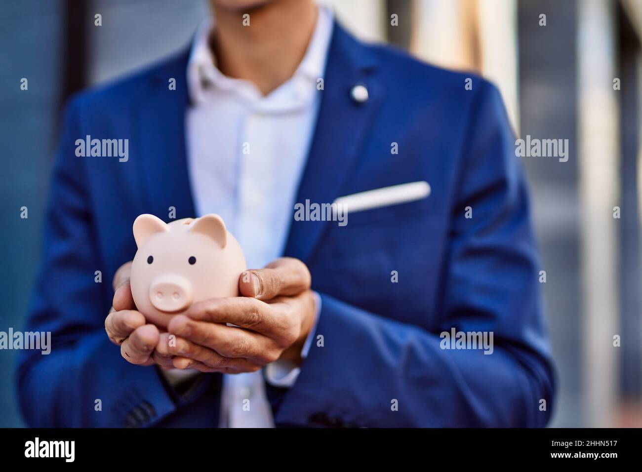 Young man wearing suit holding piggy bank at street Stock Photo - Alamy