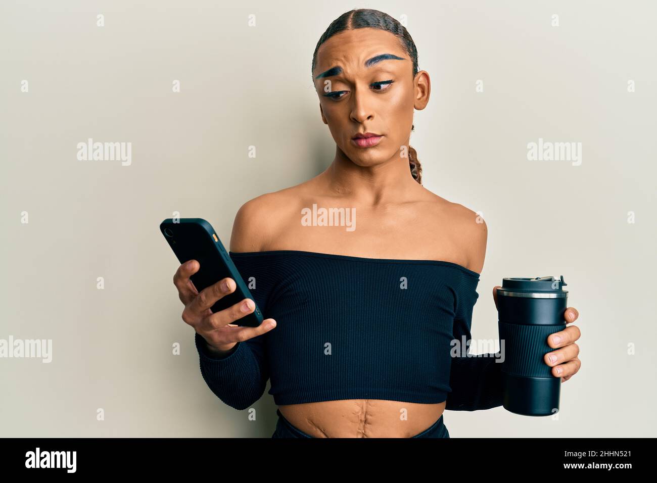 Hispanic transgender man wearing make up and long hair using smartphone ...