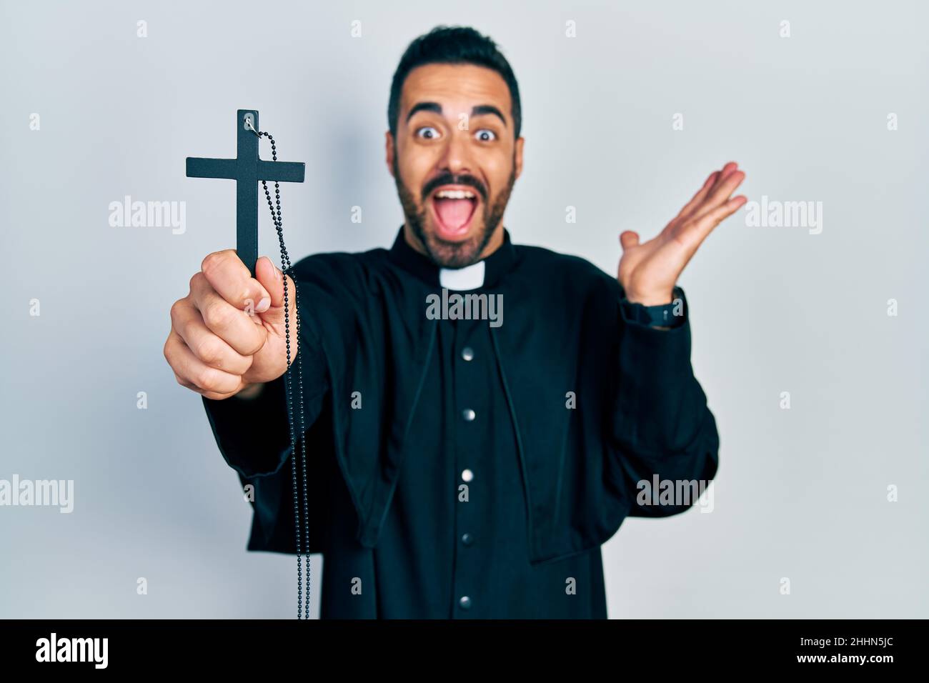 Handsome hispanic priest man with beard holding catholic cross ...