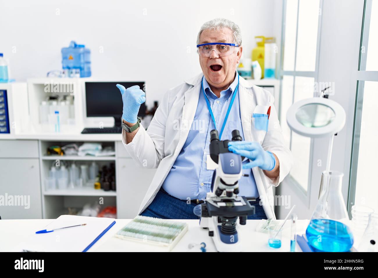Senior caucasian man working at scientist laboratory surprised pointing ...
