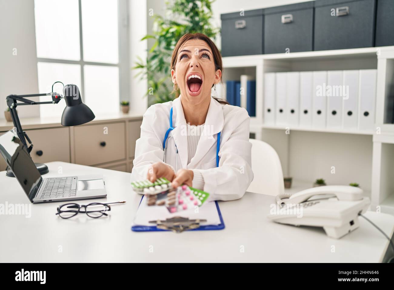 Young brunette doctor woman holding pills angry and mad screaming ...
