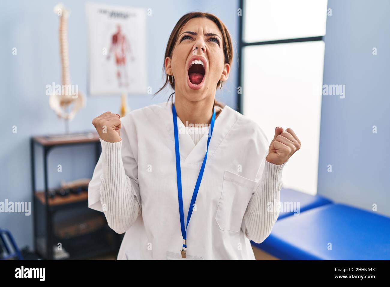 Young brunette woman working at pain recovery clinic crazy and mad ...