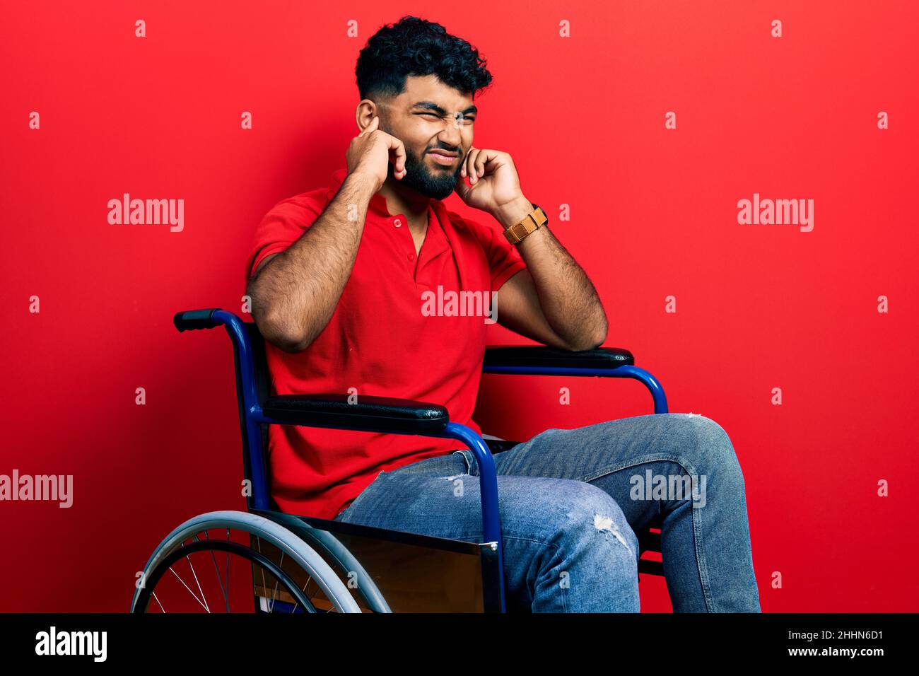 Arab man with beard sitting on wheelchair covering ears with fingers ...
