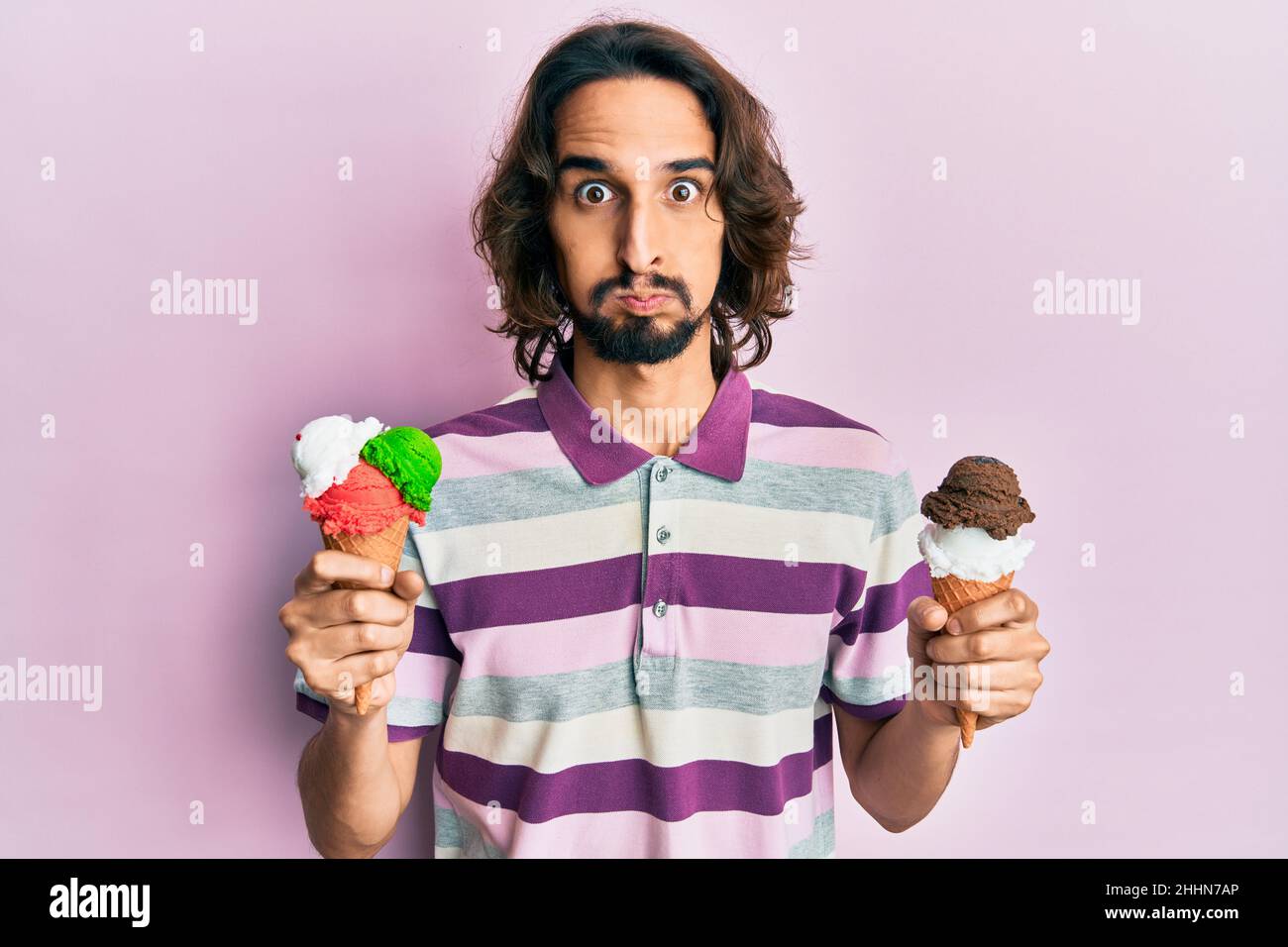 Young hispanic man holding ice cream puffing cheeks with funny face ...