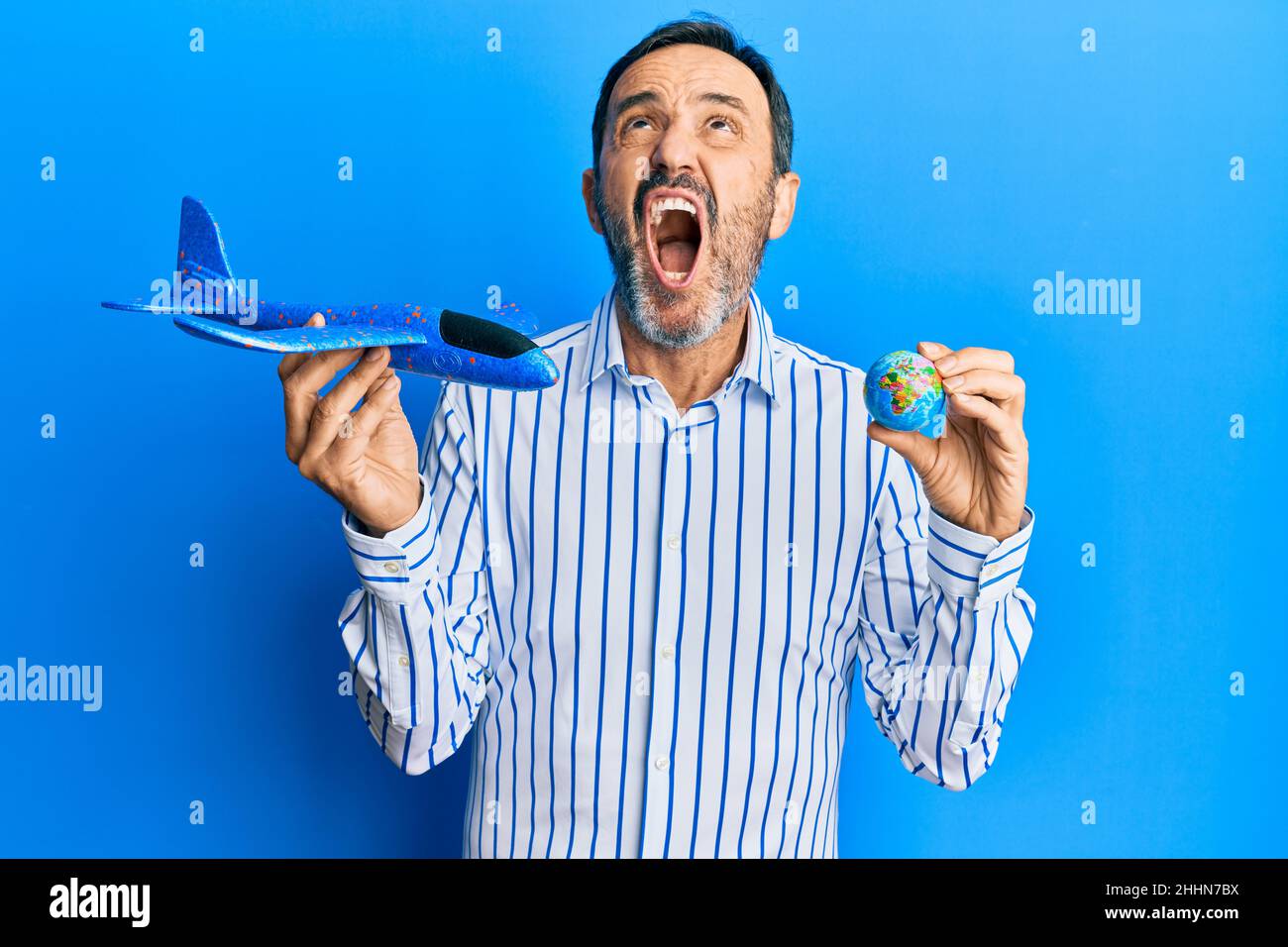 Middle age hispanic man holding plane toy and world ball angry and mad ...