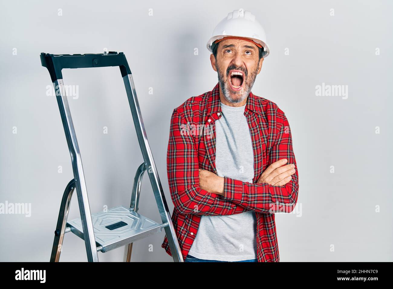 Middle age hispanic worker man with arms crossed gesture using ladder ...