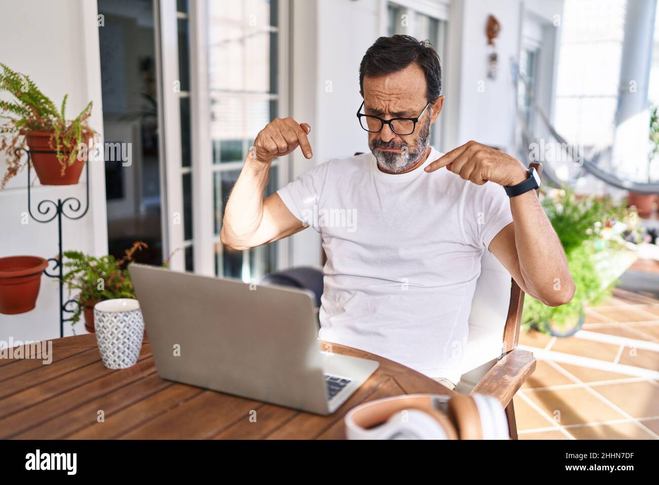 Middle age man using computer laptop at home pointing down looking sad ...