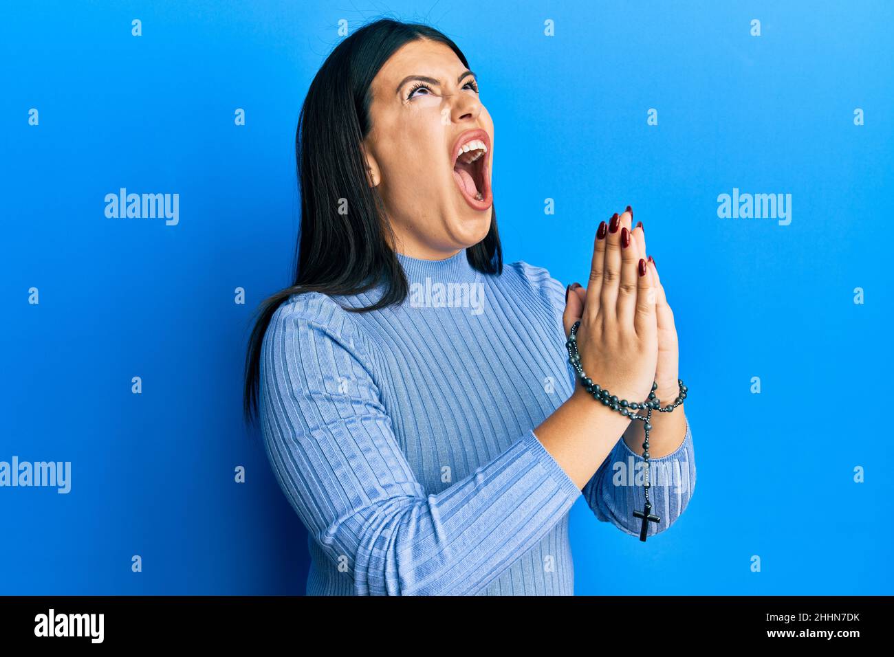 Beautiful brunette woman praying holding catholic rosary angry and mad ...