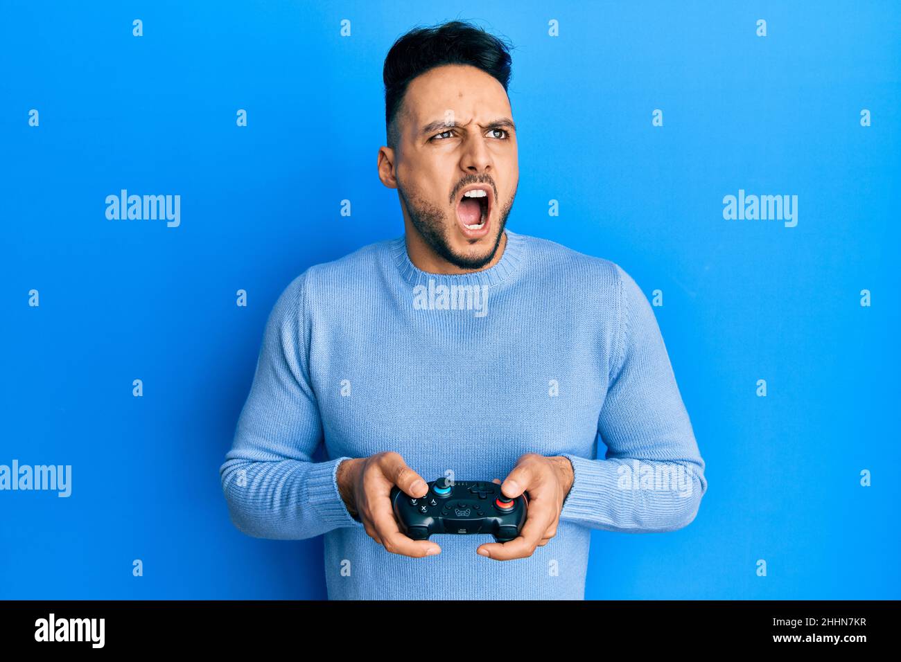 Young arab man playing video game holding controller angry and mad ...