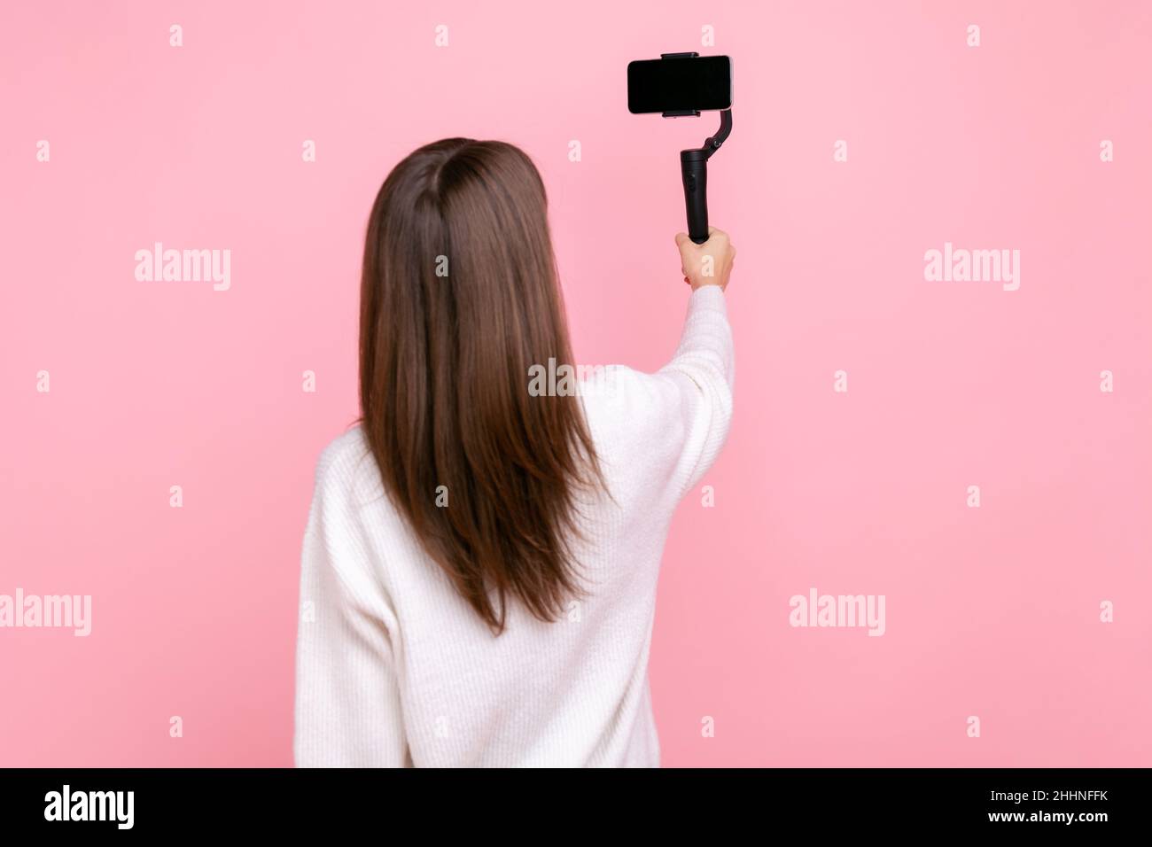 Back view of female broadcasting livestream, using steadicam and phone ...