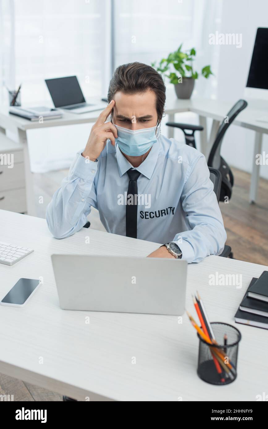 security man in medical mask looking at computer monitor near ...