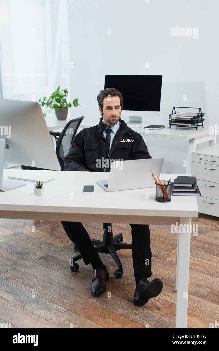 security man looking at laptop while sitting at workplace in ...