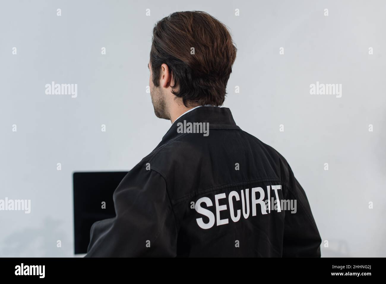 back view of guard in black uniform with security lettering in office ...
