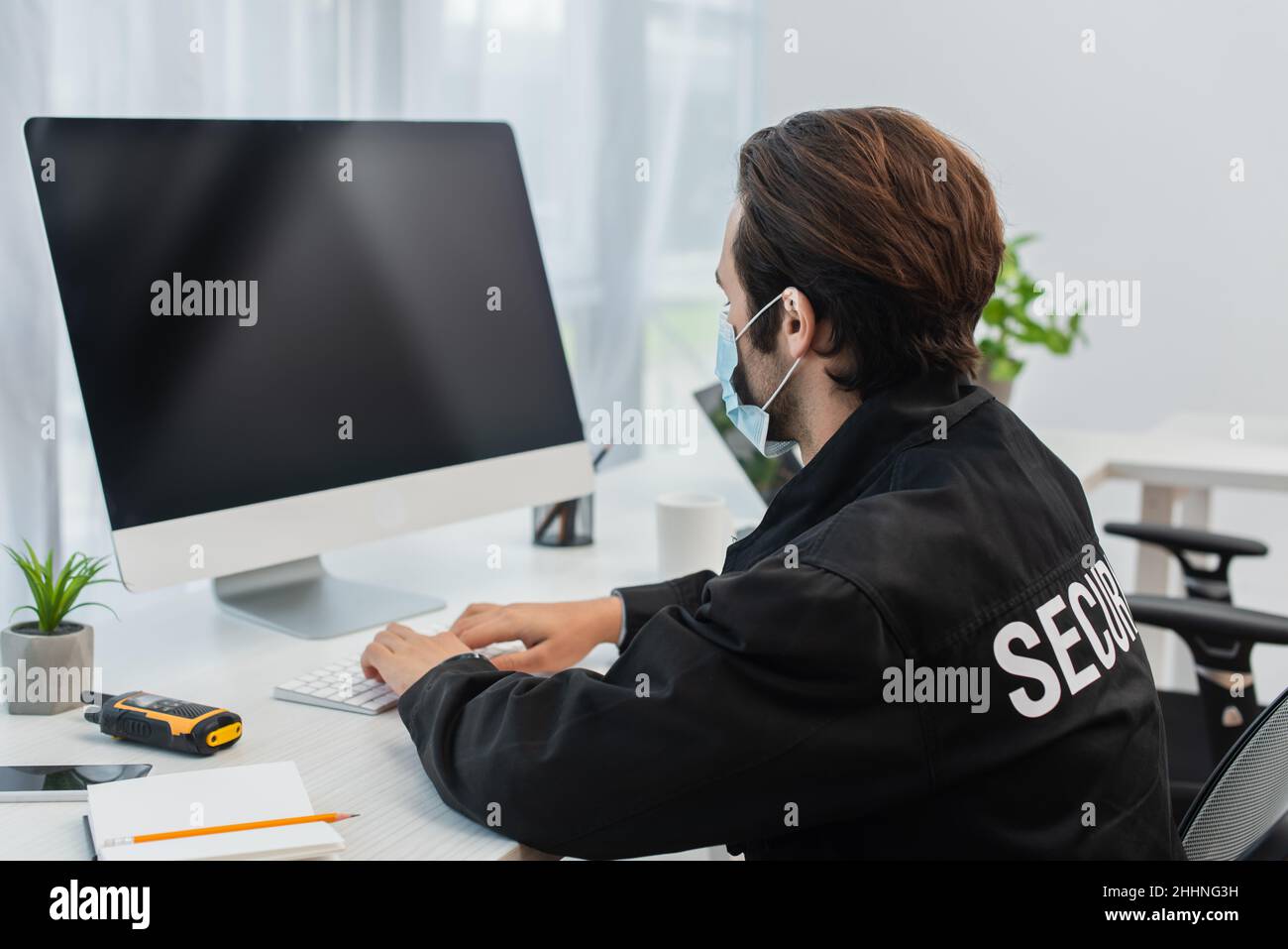 security man in black uniform and medical mask typing on computer in ...