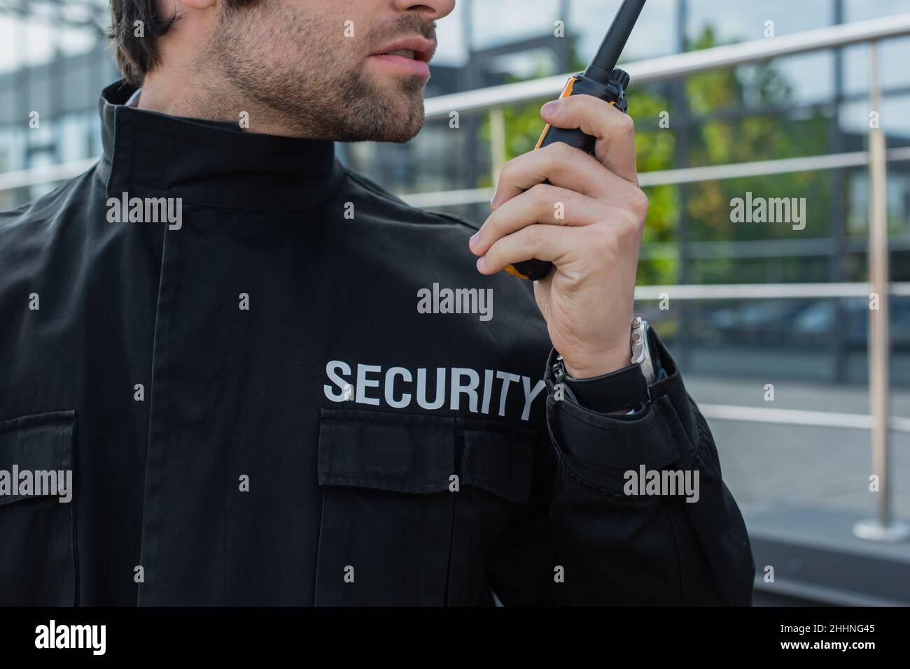 partial view of guard in uniform with security lettering talking on ...