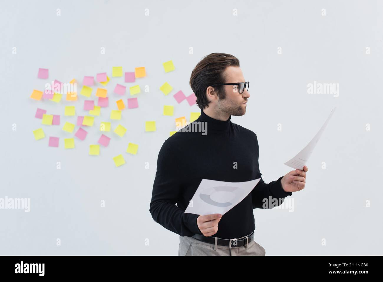 displeased man looking at documents near sticky notes on grey wall ...