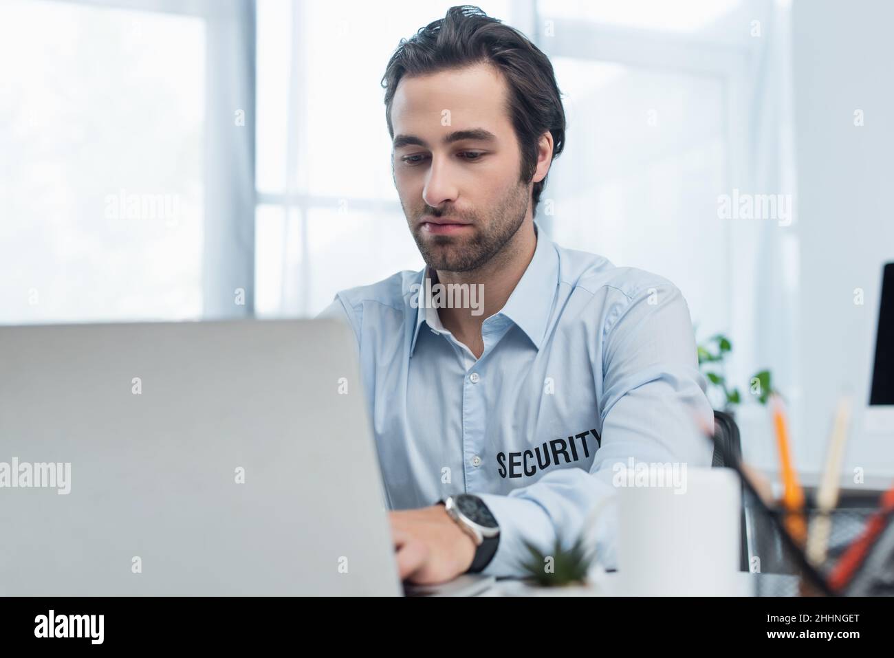 security man typing on blurred laptop while working in supervision room ...