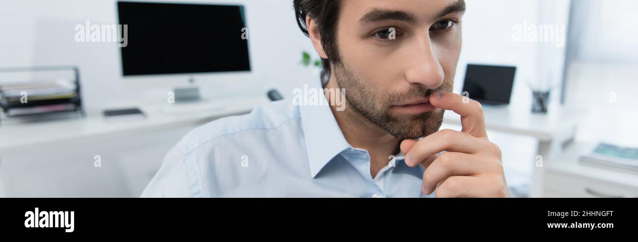pensive businessman touching lips while thinking near computers on ...