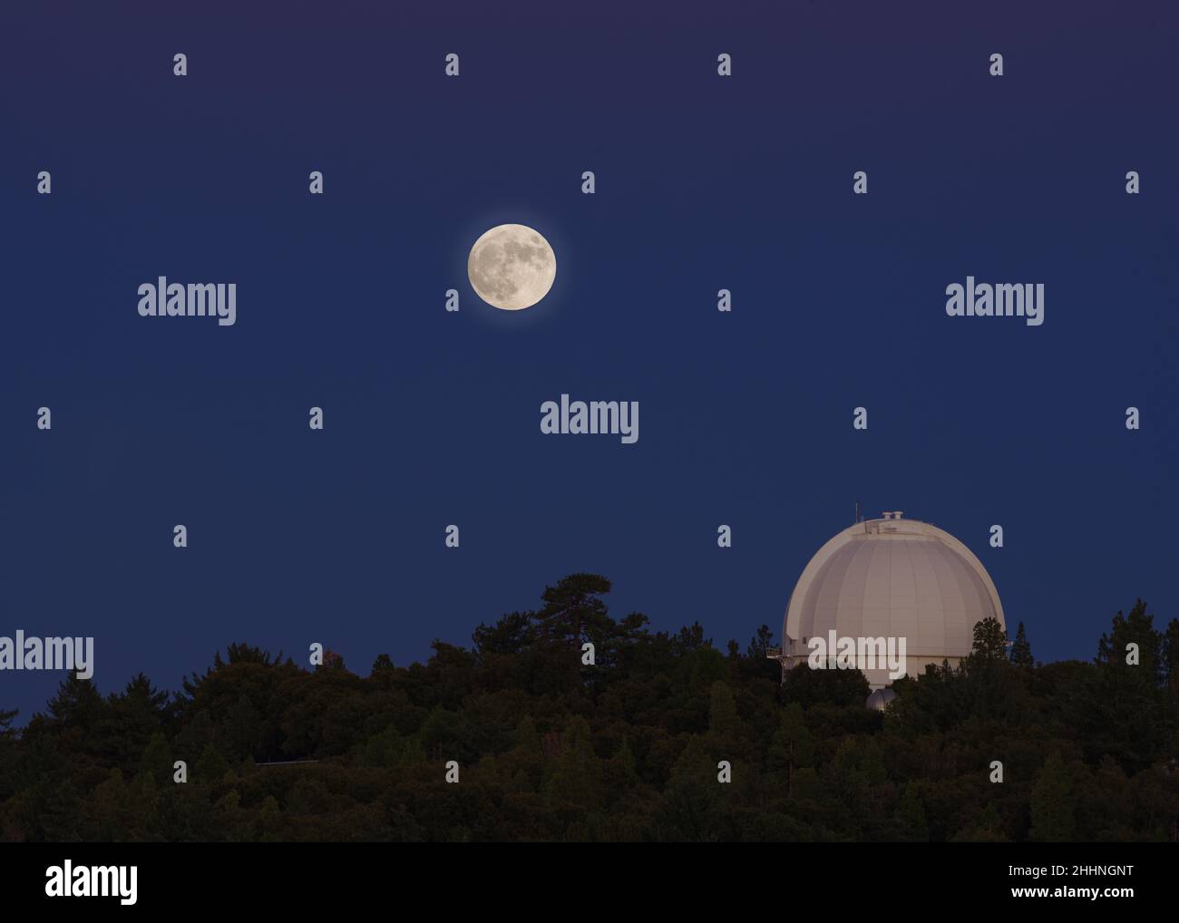 Full moon rising over astronomical observatory against a deep blue ...
