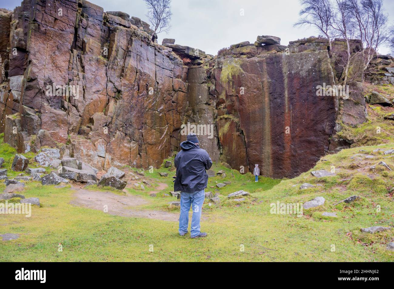 A man photographs his daughter loking tiny benath the sheer raock face ...