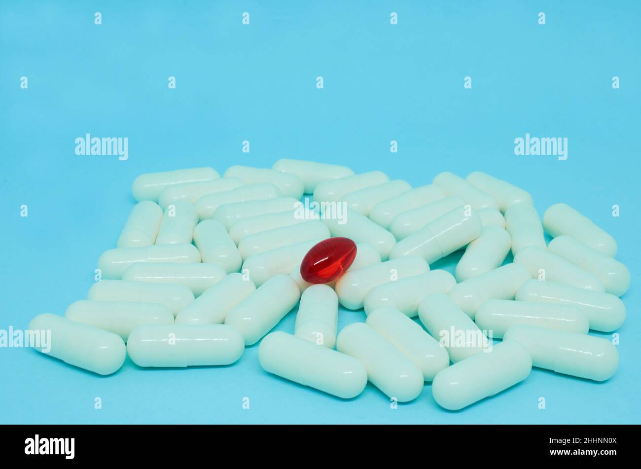 Many white capsules and one dark red capsule are scattered on a blue ...