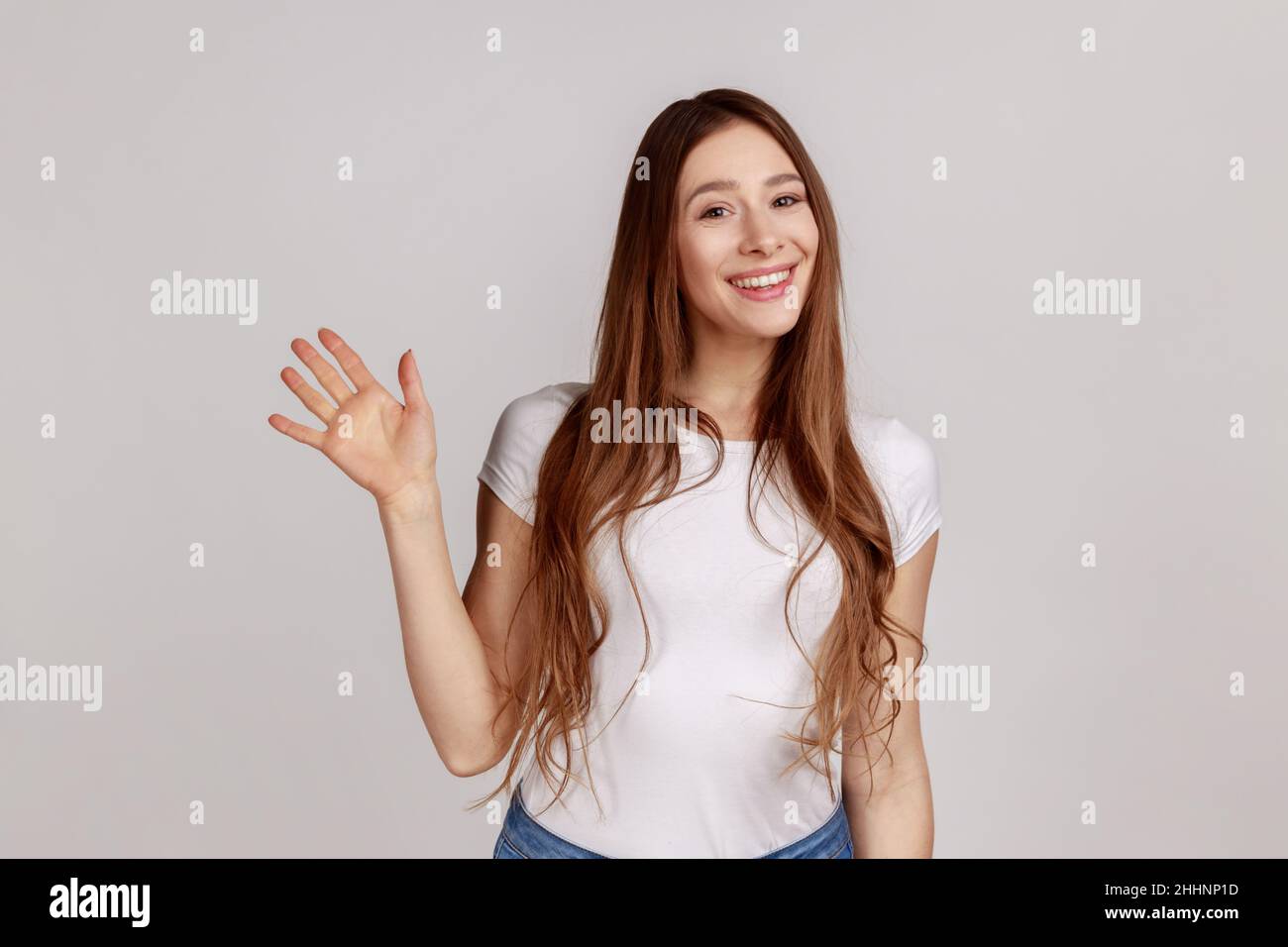 Hello. Portrait of happy woman standing with raised hand saying hi to ...