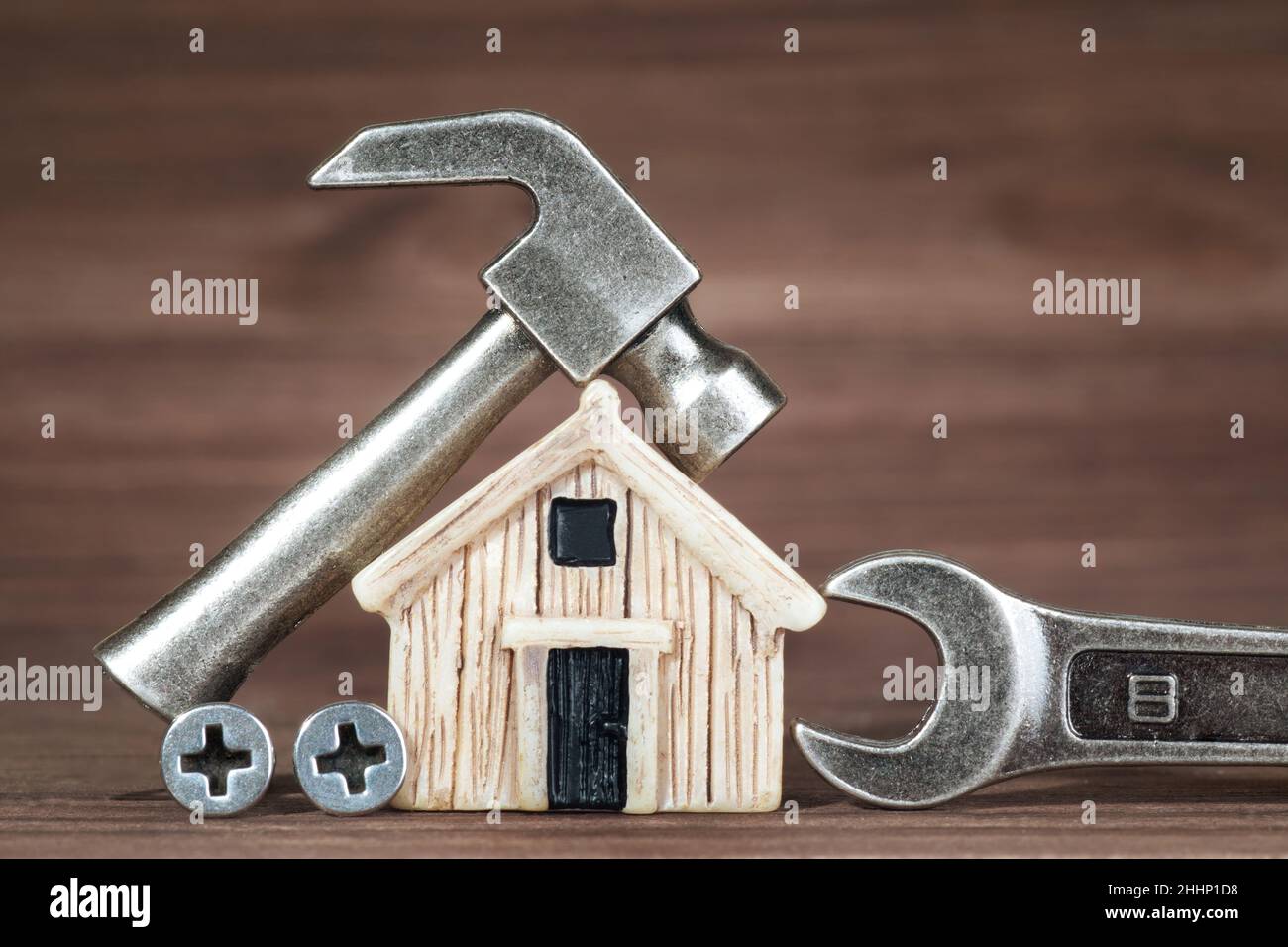 Miniature house and small hand tools with screws against a wooden ...