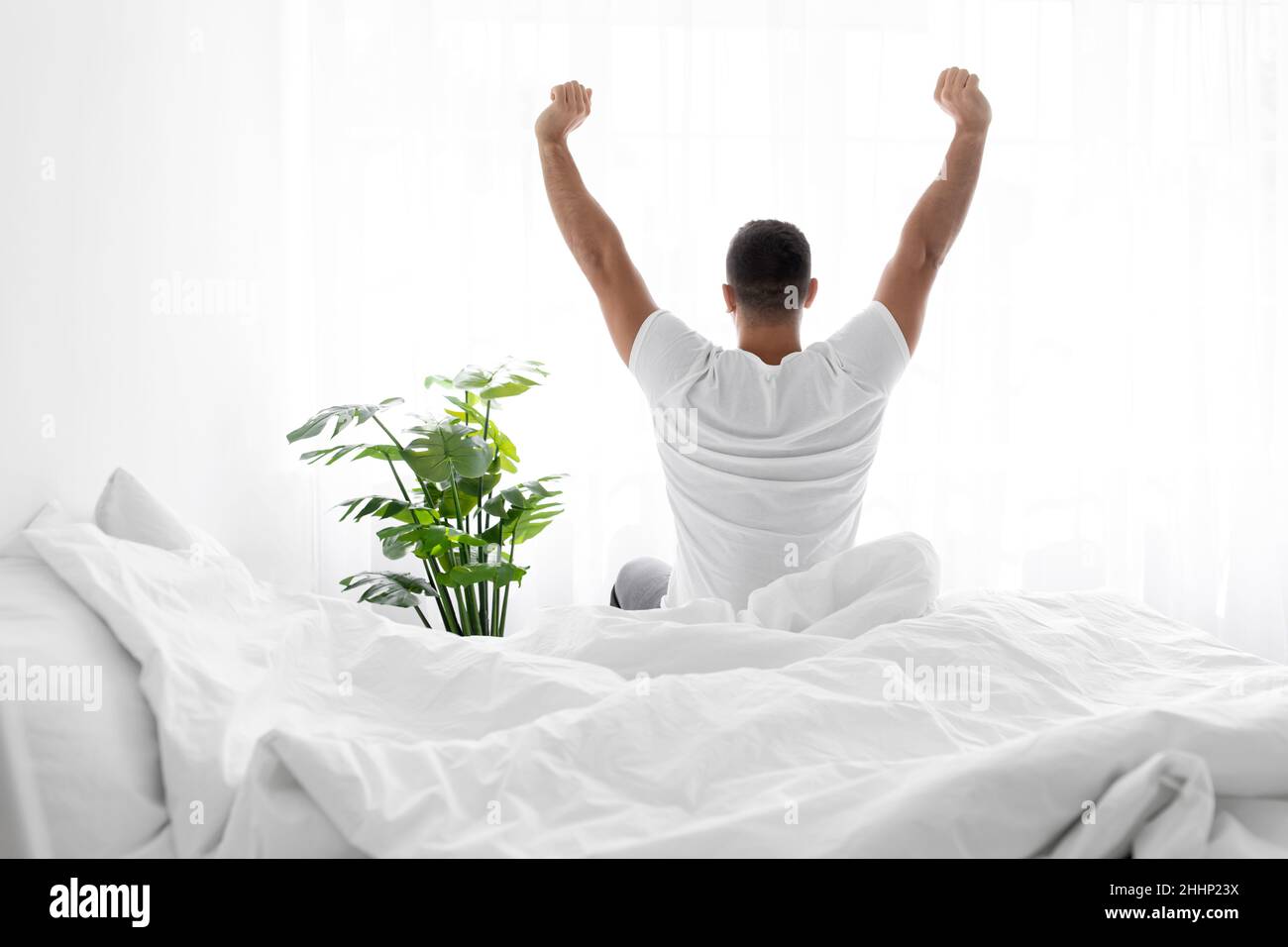 Happy young caucasian muscular man sits on white bed, wake up ...