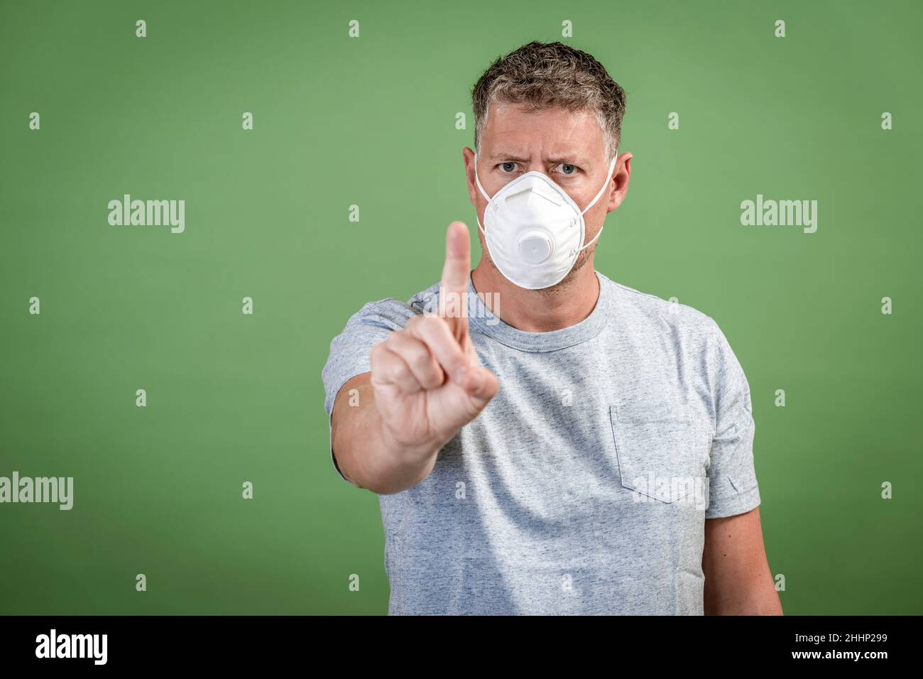 man with ffp2 nose and mouth mask standing in front of green background ...