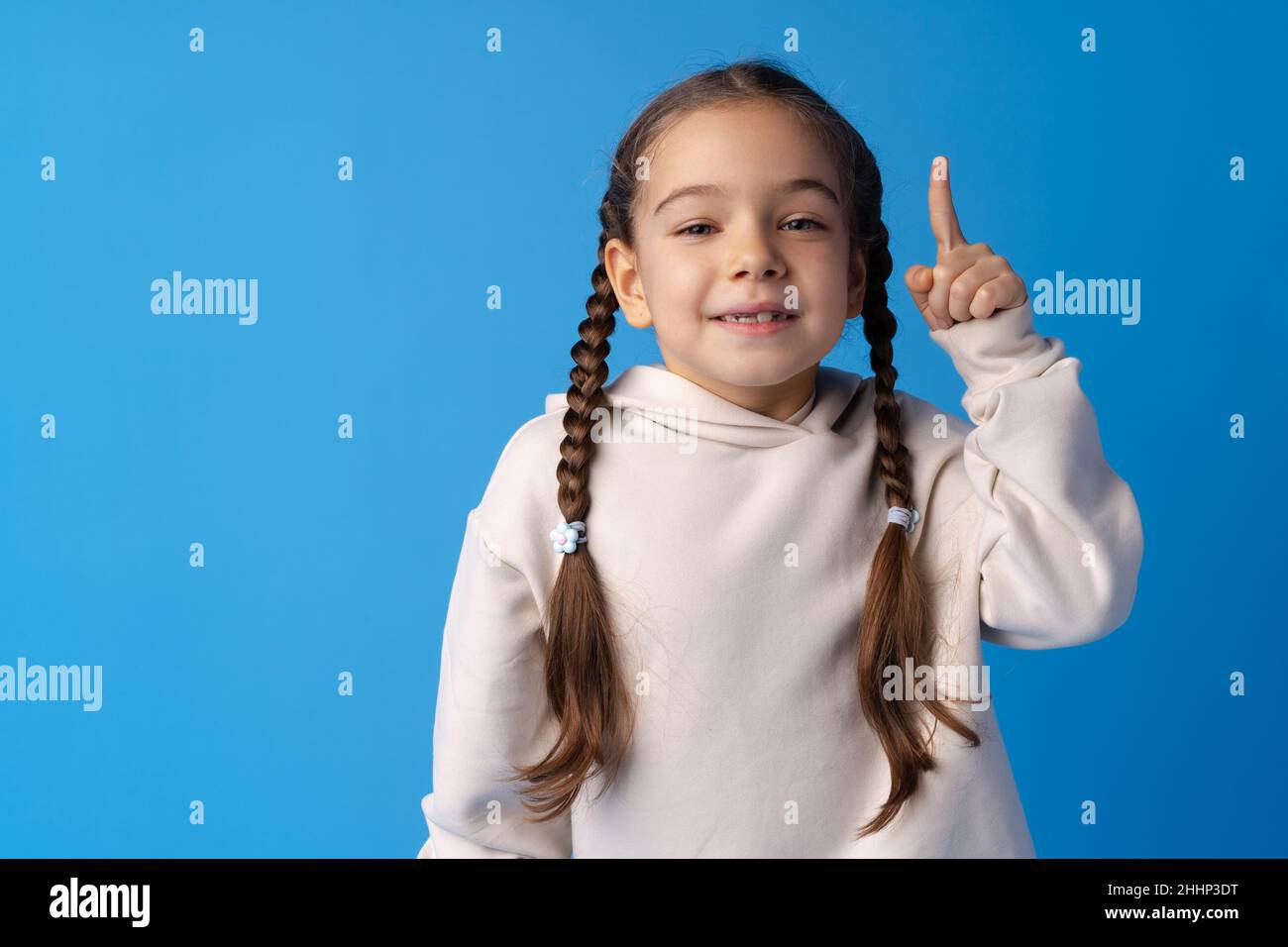 Cute little girl pointing up and having idea against blue background ...