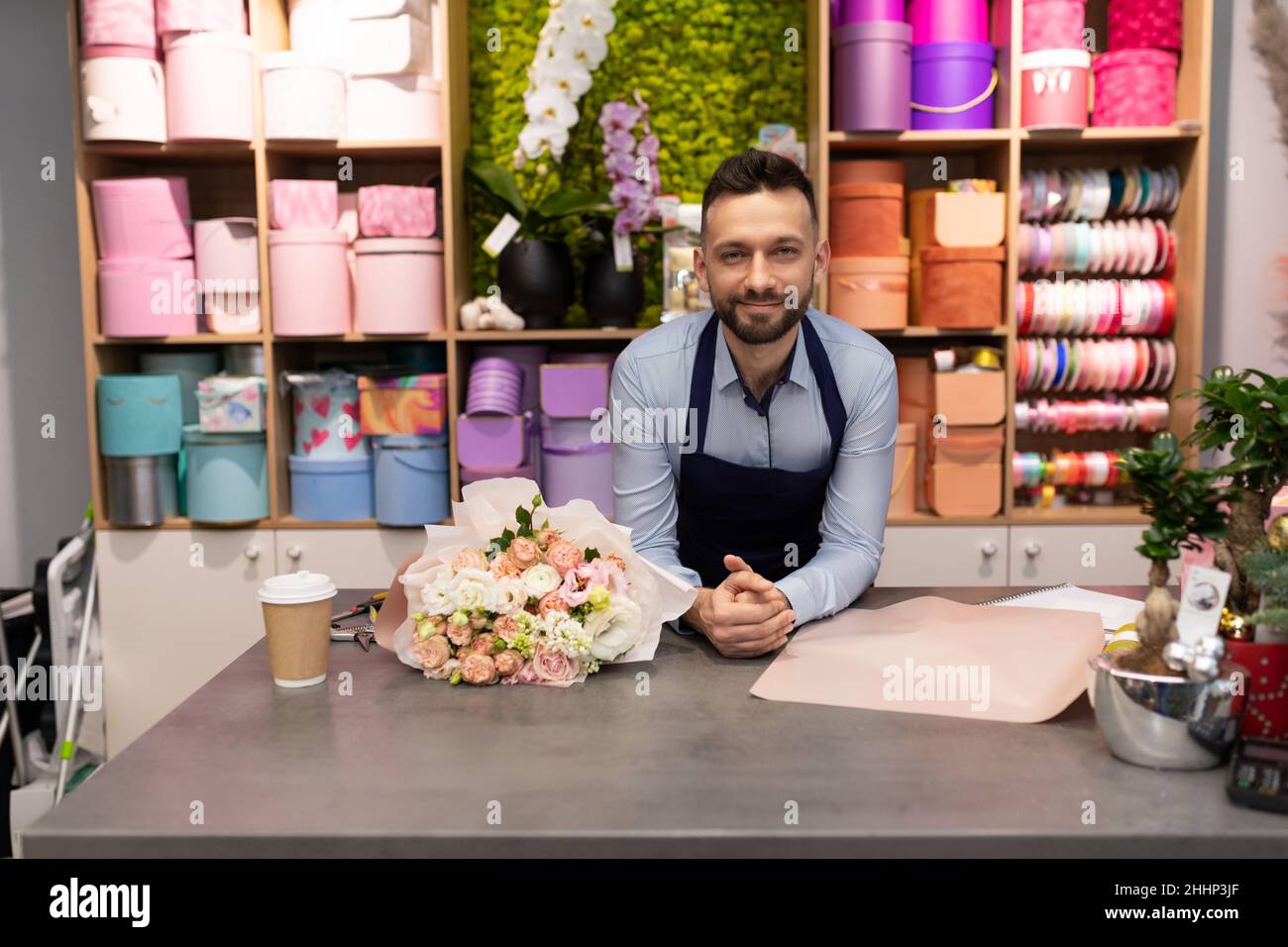 male florist in a flower shop behind the counter next to a bouquet ...