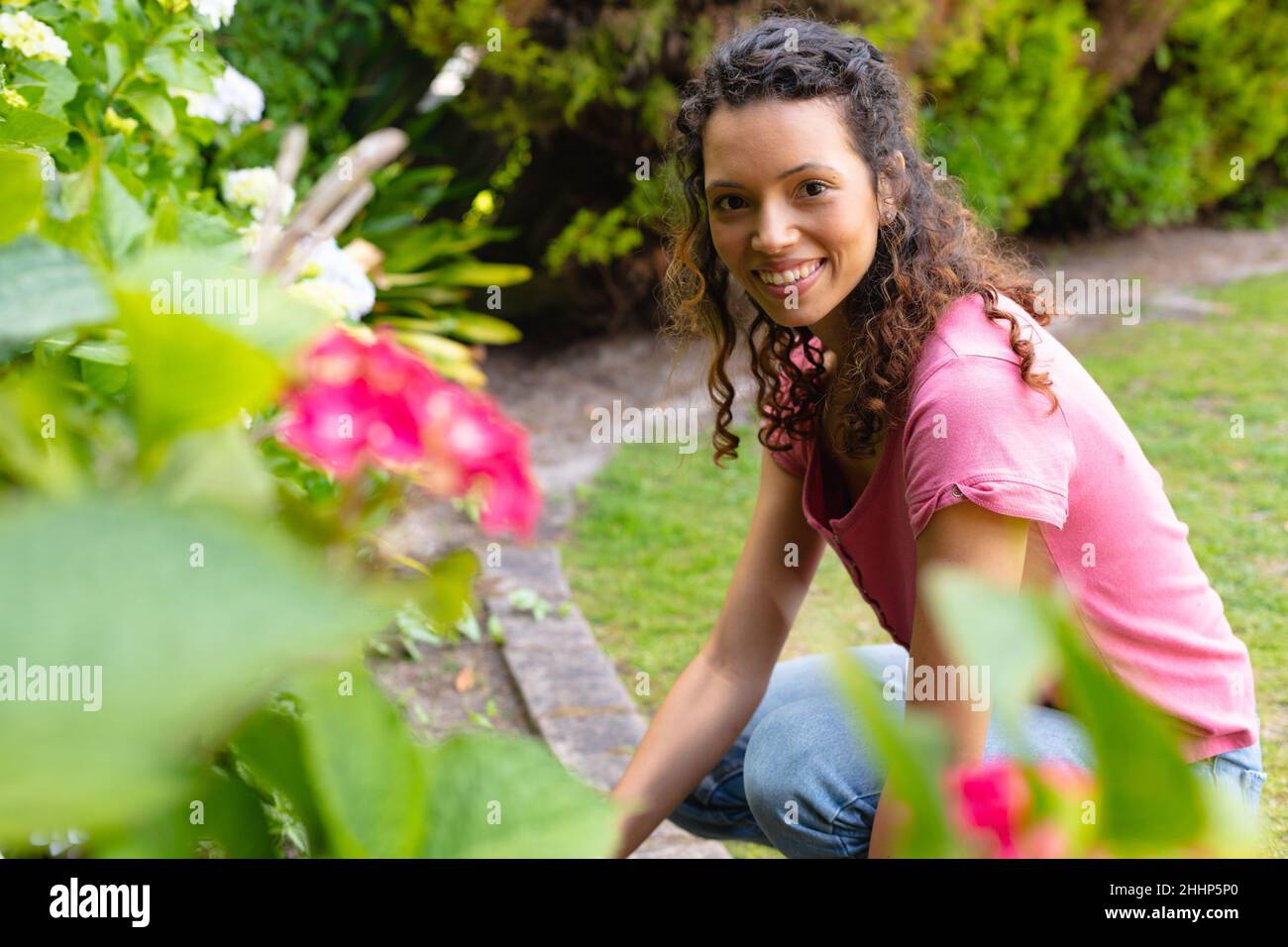 Portrait of smiling young biracial woman with curly hair gardening in ...