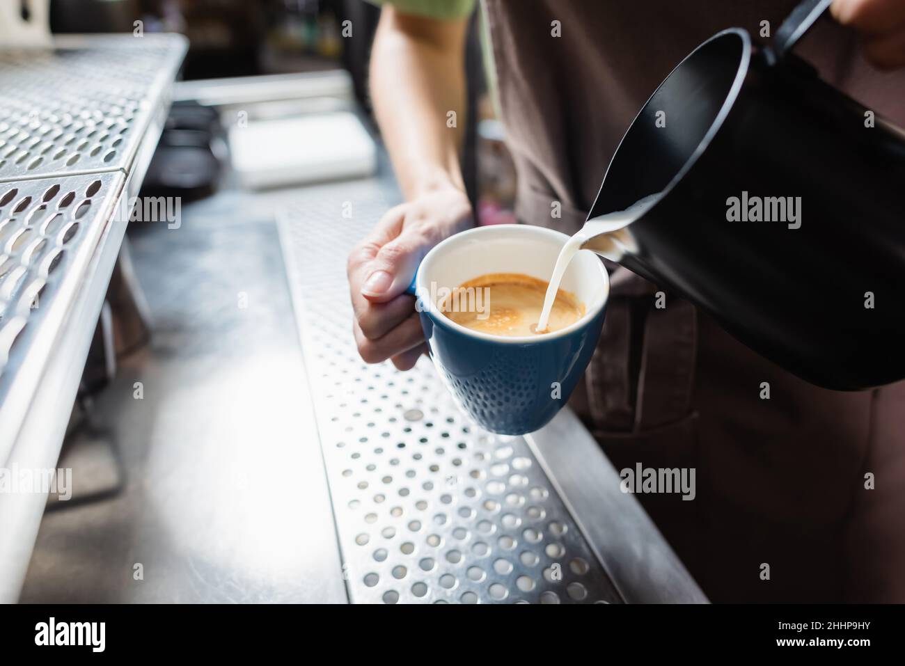 Cropped view of barista pouring milk in cup with coffee in cafeteria ...
