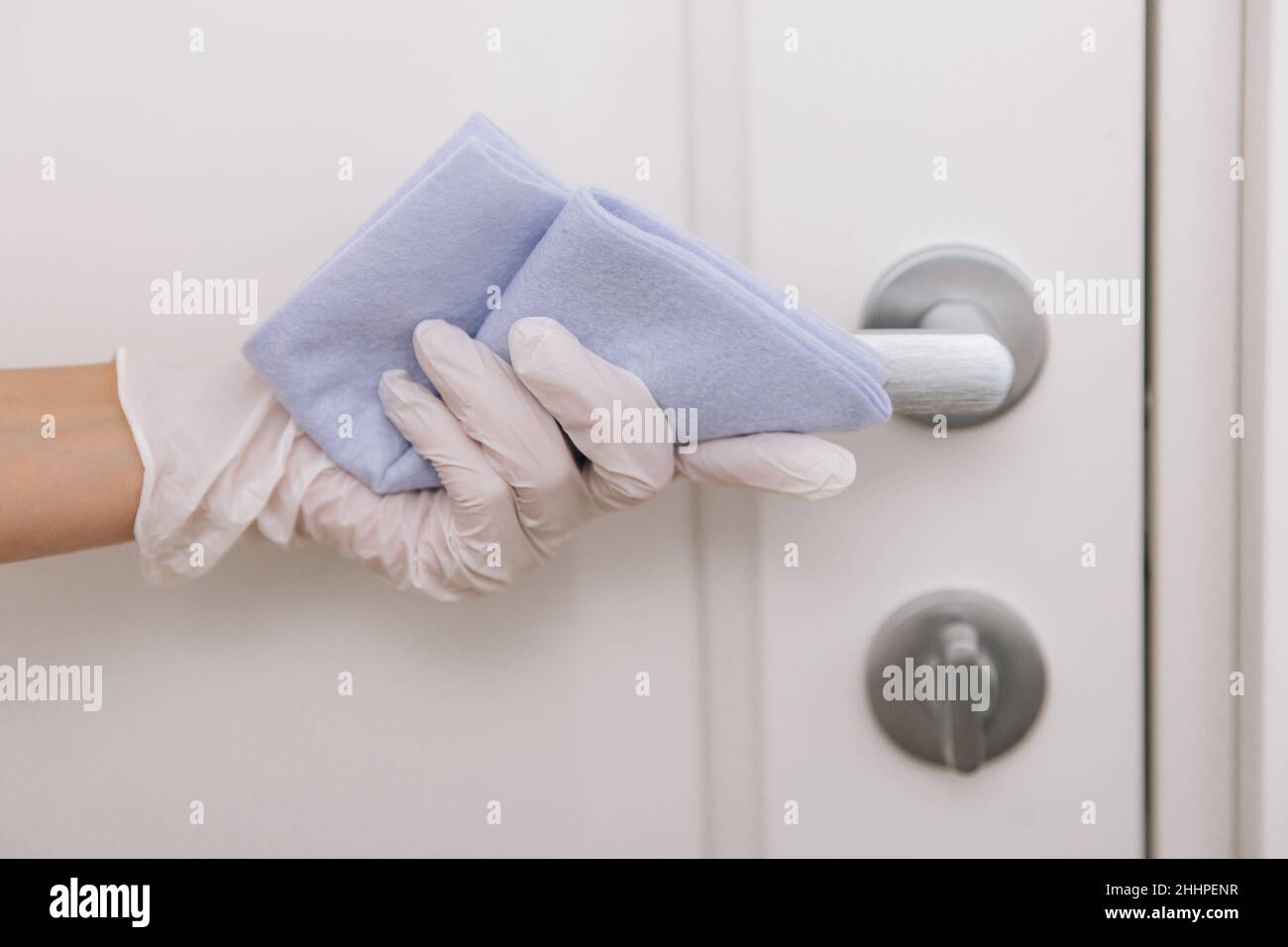 Cleaning door handle with blue wipe in white gloves. Woman hand using ...