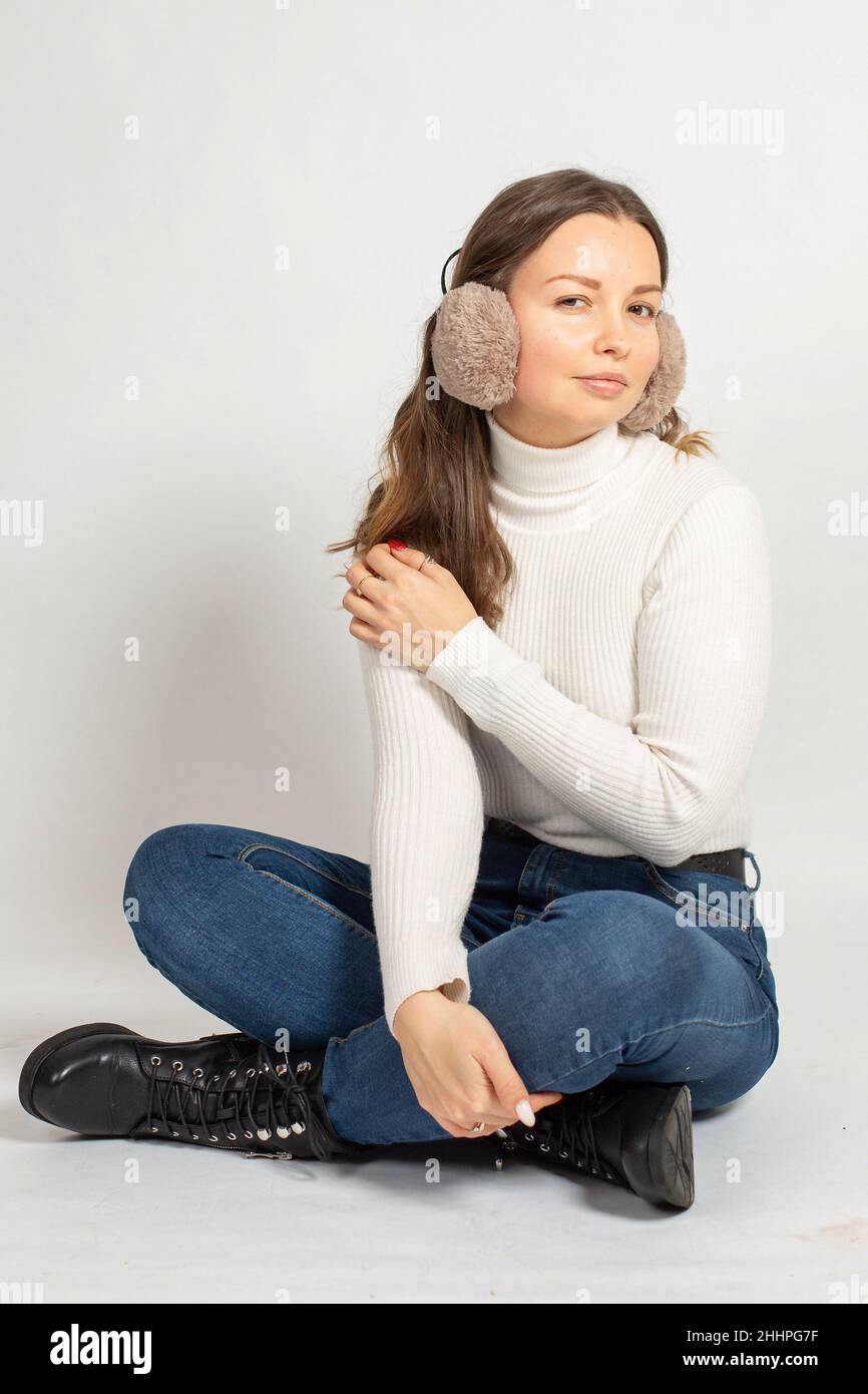 Young woman in warm white jumper with fur earmuffs isolated on white ...