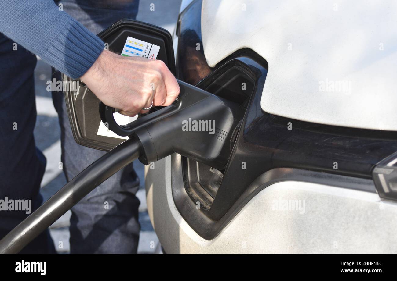 The hand and arm of a man holding an electric vehicle cable as he plugs ...