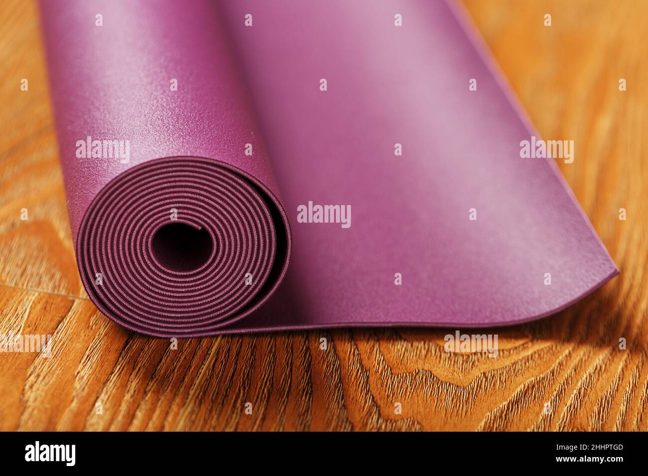 An unfolded lilac-colored yoga mat is unfolded on the wooden floor. Top ...