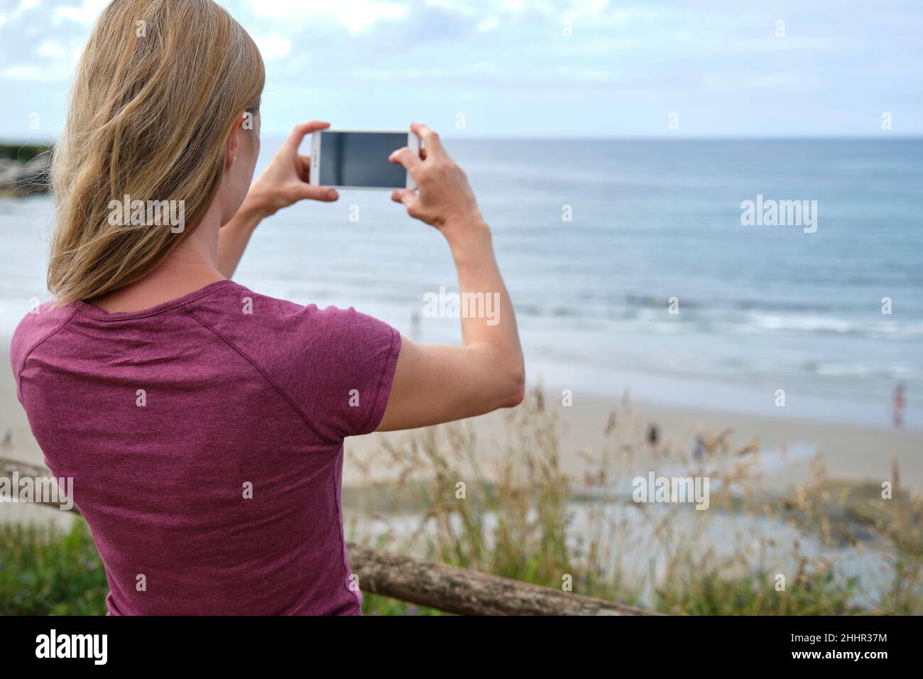Woman taking photograph with smart phone camera on the beach, Back view ...