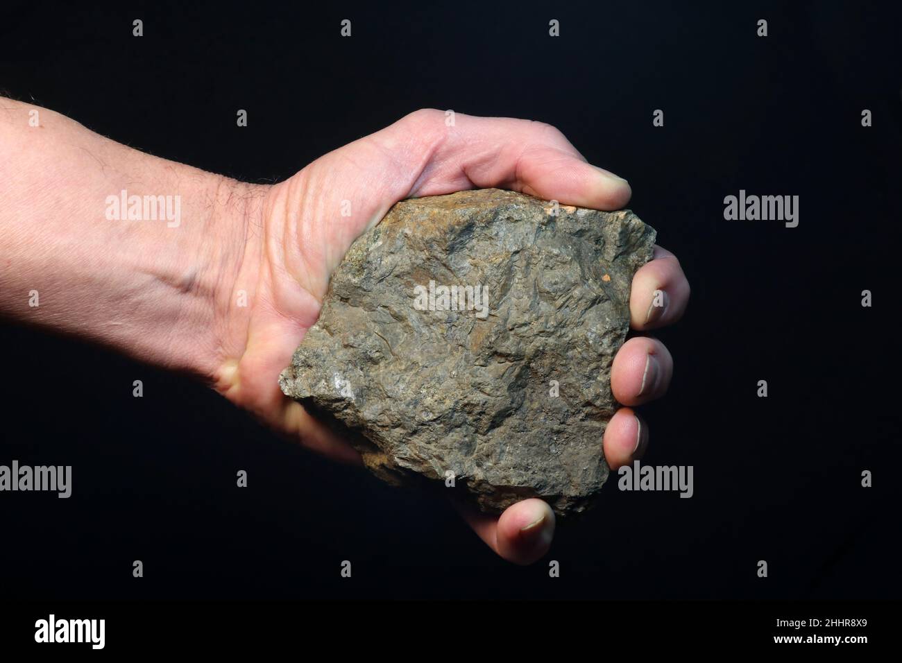 Hand holding a large stone on black background Stock Photo - Alamy